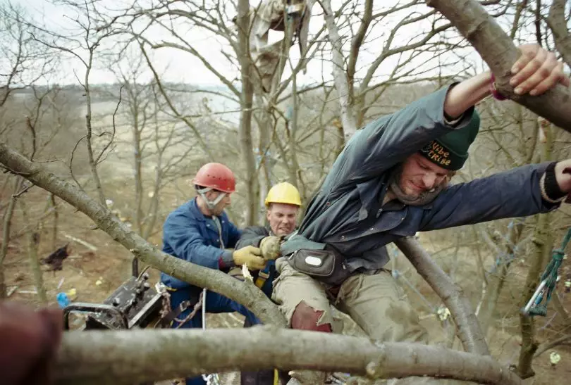 Newbury Bypass 1996: a 60 peus sobre el terra, un home intenta desesperadament penjar-se a l'arbre per protegir-lo de ser tallat mentre és tirat cap enrere pels homes del xèrif de Newbury.