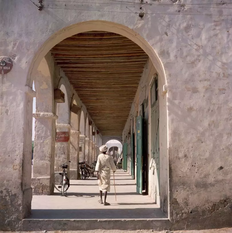 Sudão, 1958 – Homem andando por lojas ao longo de uma colunata em arco © 2021 Todd Webb Archive