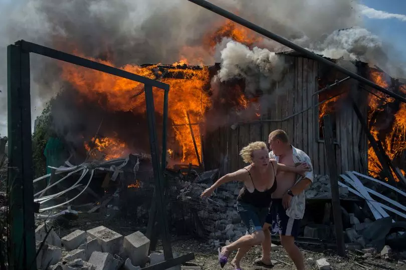 Civili evadează dintr-un incendiu la o casă distrusă de un atac aerian în Donbass, un sat din Luhanskaya, estul Ucrainei, pe 2 iulie 2014. © Valery Melnikov. Câștigător pentru Fotojurnalism Single Image, Magnum and LensCulture Photography Awards 2016