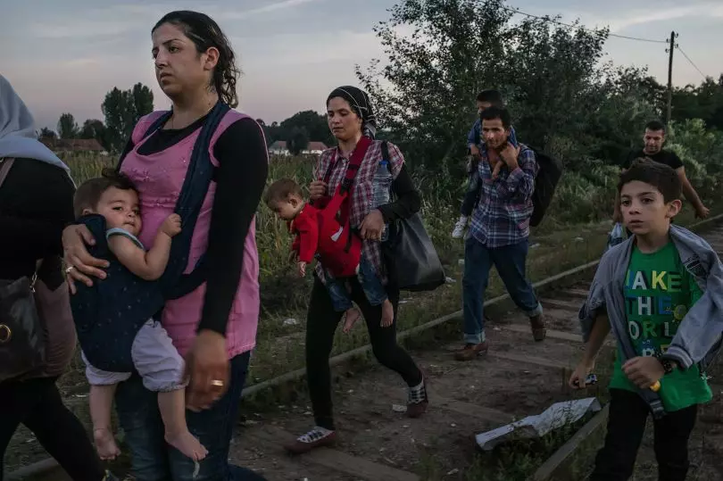 Horgos, Serbi, 30 gusht 2015. Në muzg, Roujin Sheikho, në të majtë, mban vajzën e saj Widad e ndjekur nga djali i saj Nabih, në të djathtë. Ky grup ecën mes refugjatëve të tjerë nga Siria, të cilët lejohen të kalojnë telat me gjemba në errësirë për në Hungari, në rrugën e tyre të gjatë për në Suedi. © Mauricio Lima. Fituesi i Serive Dokumentare, Çmimet e Fotografisë Magnum dhe LensCulture 2016