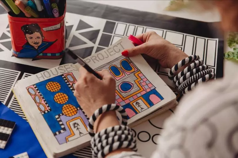 Shot fan Camille Walala tekene yn har sketsboek yn har atelier, wurke oan 'e nij lansearre ynstallaasje foar LEGO DOTS. Foto credit Dunja Opalko.