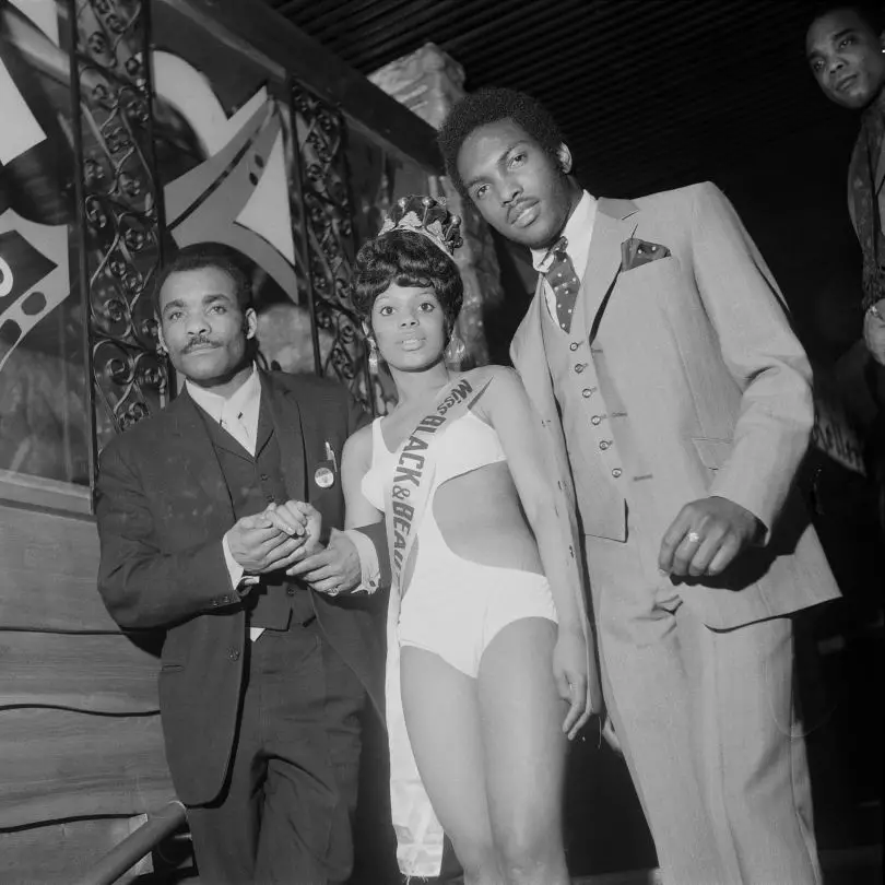 (hajatambulika) Miss Black & Beautiful akisindikizwa na wanaume wawili, Hammersmith Palais, London, 1970s. Kutoka kwingineko 'Black Beauty Pageants'. © Raphael Albert, kwa hisani ya Autograph ABP