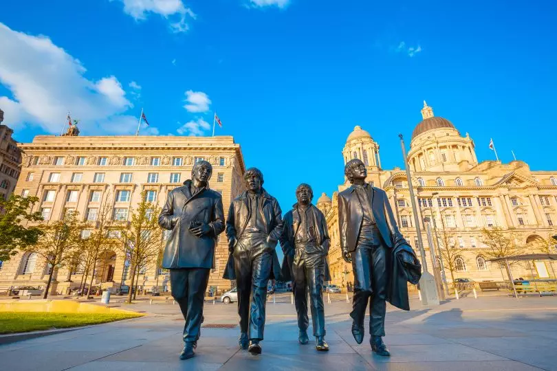 Patung Perunggu Beatles ngadeg ing Pier Head ing pinggir Kali Mersey, sing diukir dening Andrew Edwards. Gambar dilisensi liwat Adobe Stock / Miturut Coward Lion