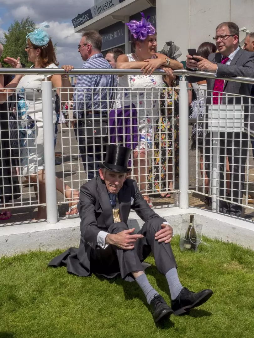 En äldre herre i högtidlig klädsel satt på gräset och tittade på hästkapplöpningen från The Queen's Stand under Epsom-festivalen. Juni 2018 © Peter Dench