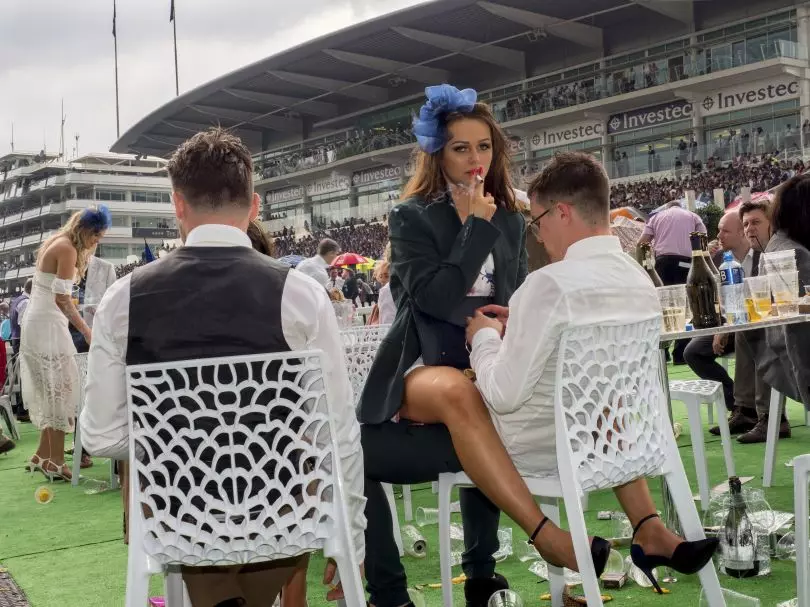 En ung kvinna röker en cigarett gränsad över en mans knä på Ladies Day på Epsom. Juni 2017 © Peter Dench